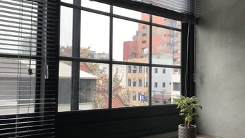 Uma janela com persianas, um vaso de planta em um peitoril e vista para edifícios lá fora.