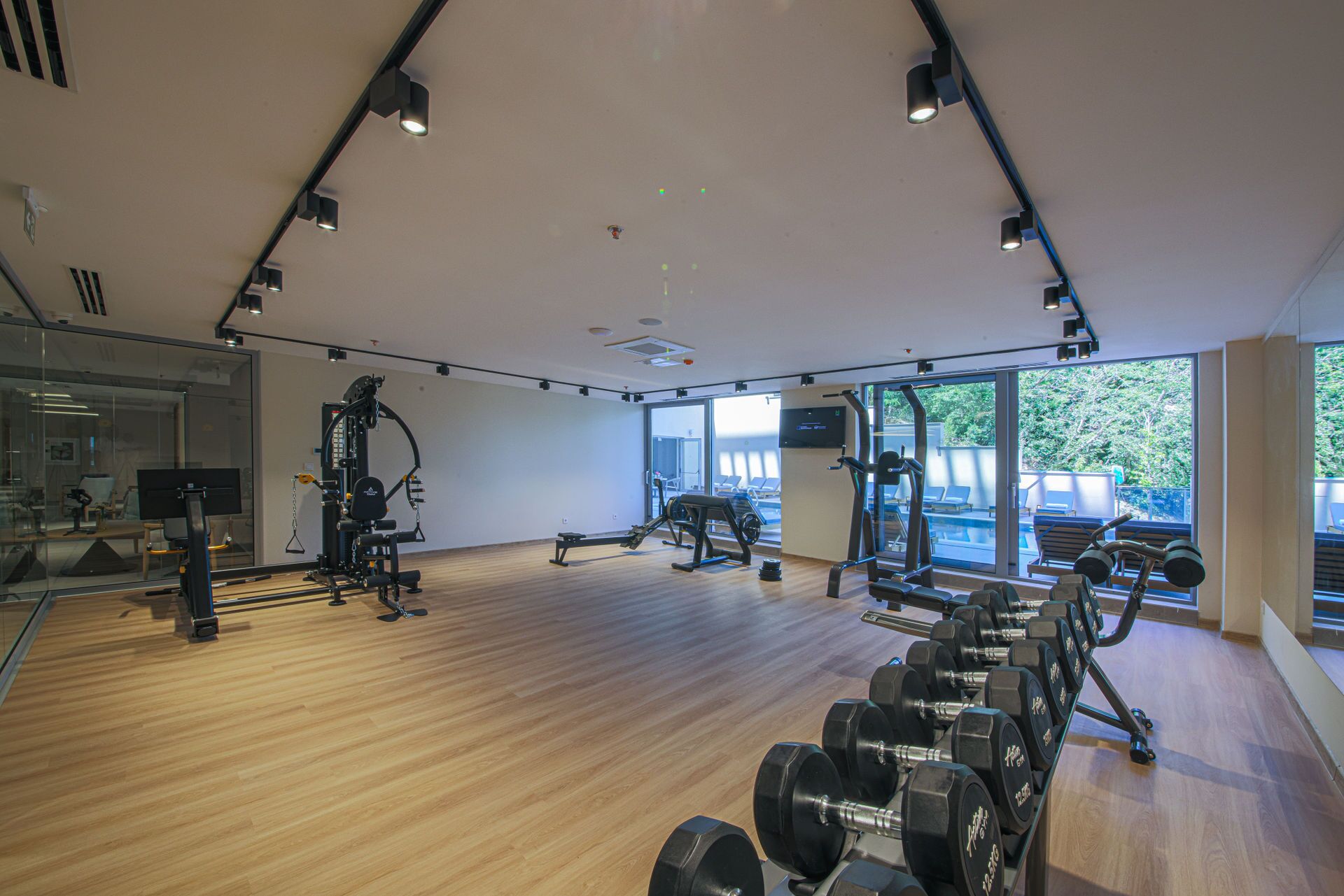 Uma academia moderna com diversos equipamentos de exercício, janelas amplas e piso de madeira.