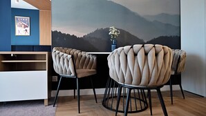 Quarto com um grande mural de montanhas, duas poltronas estofadas, uma mesa pequena e um vaso azul com flores.
