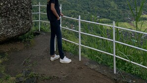 Uma pessoa em um afloramento rochoso, com vista para um vale verde e uma cidade distante.