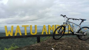 Uma bicicleta de montanha estacionada em frente a uma placa com o texto 'WATU AMEN'.