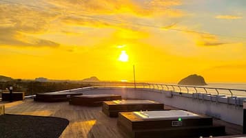 Terraço no telhado com piso de madeira, áreas de estar e vista para o pôr do sol sobre o oceano.