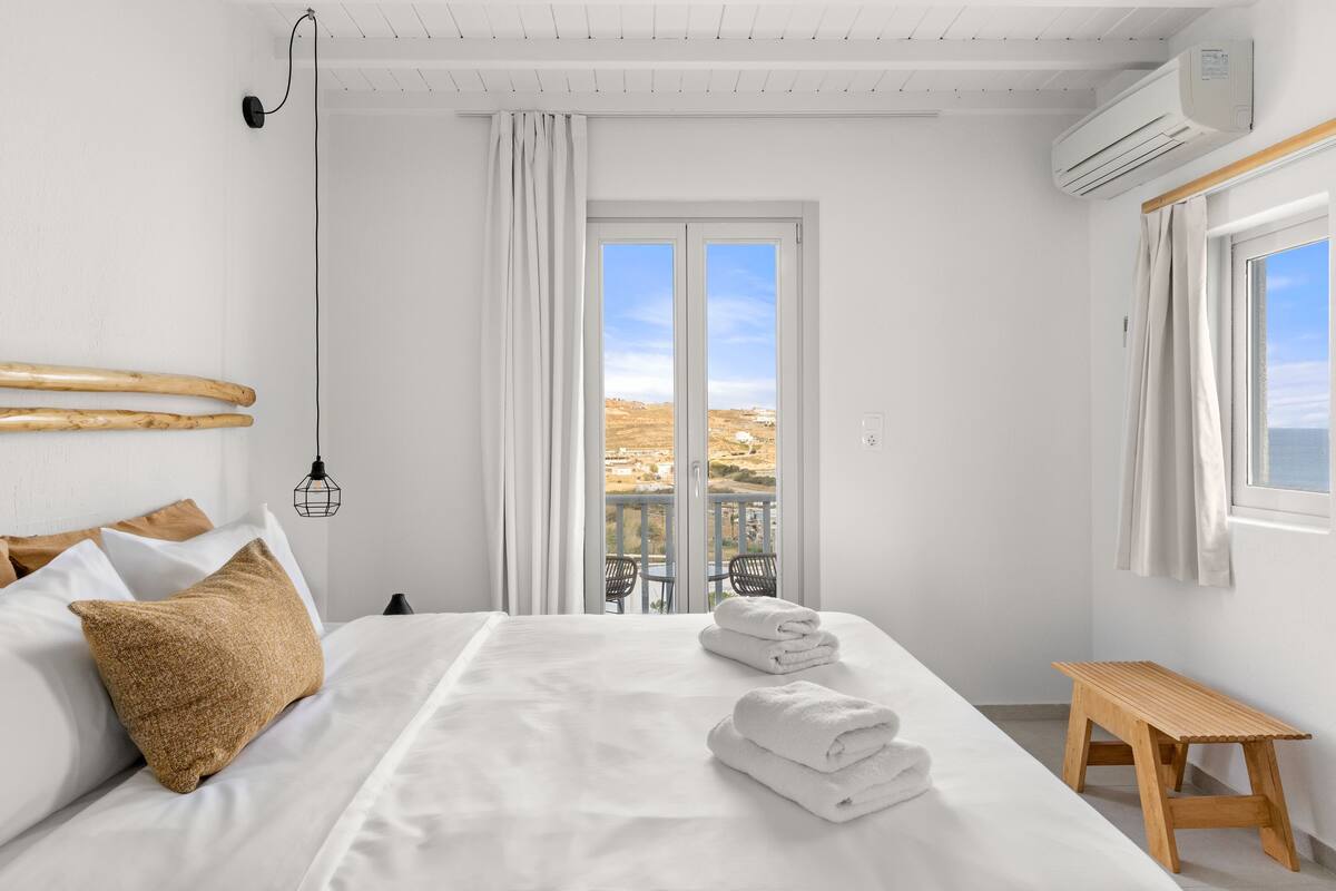 Quarto de hotel com cama, um banco de madeira, vista do campo e ar condicionado.