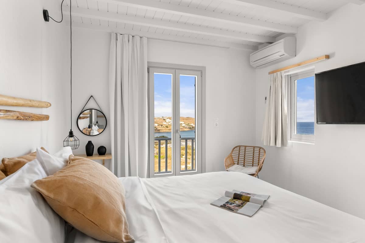 Quarto com cama, uma cadeira, janela com vista e televisão.