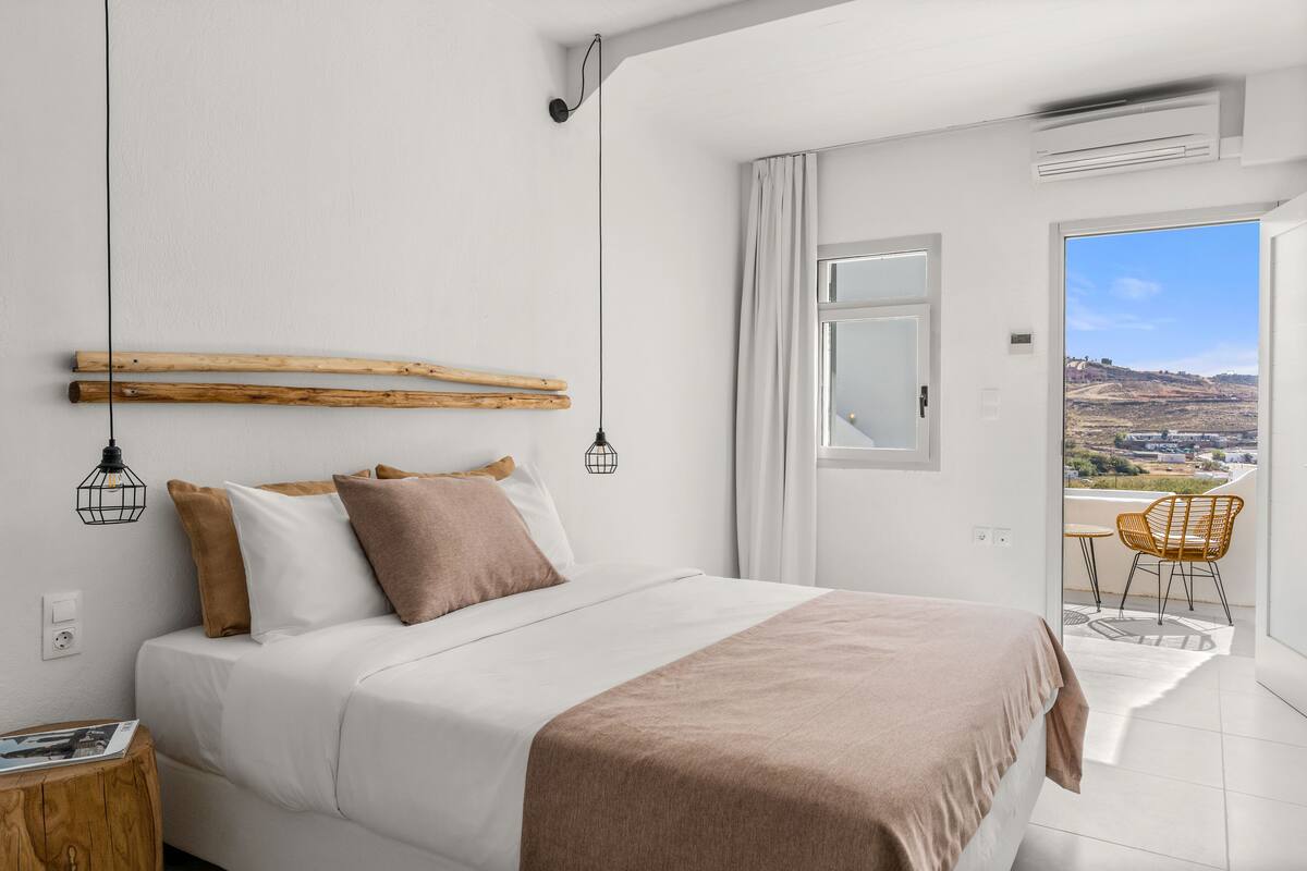 Quarto com cama, cabeceira de madeira, mesa de cabeceira, janela e vista para o exterior.