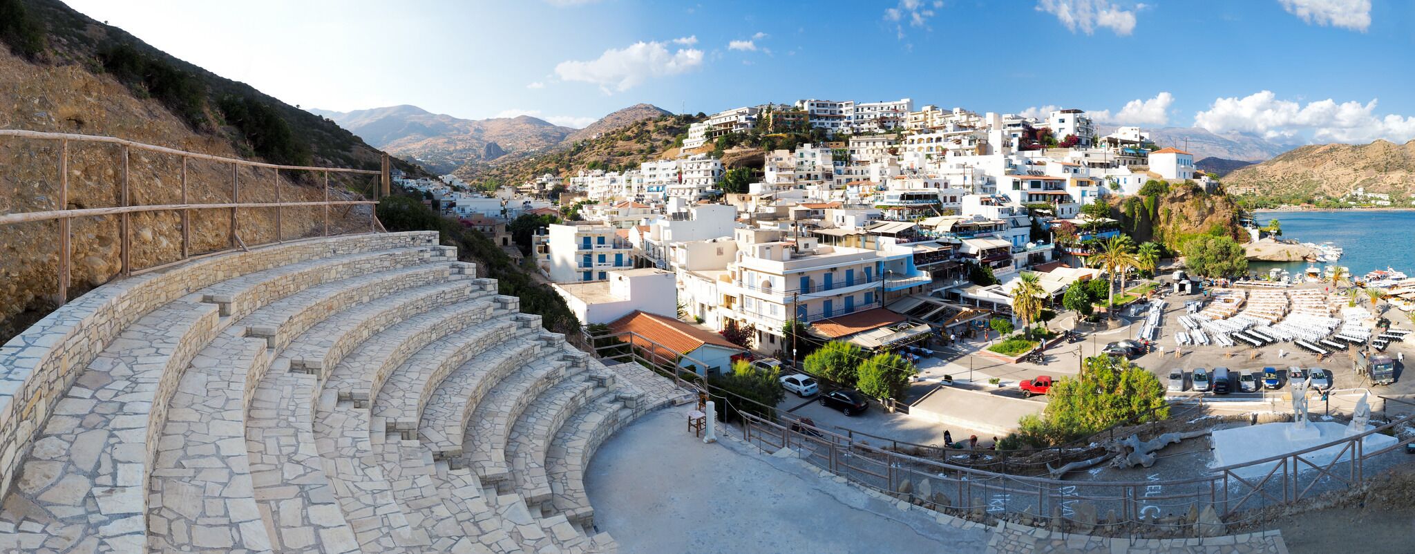 Uma vila costeira com um anfiteatro de pedra, edifícios brancos e uma marina.