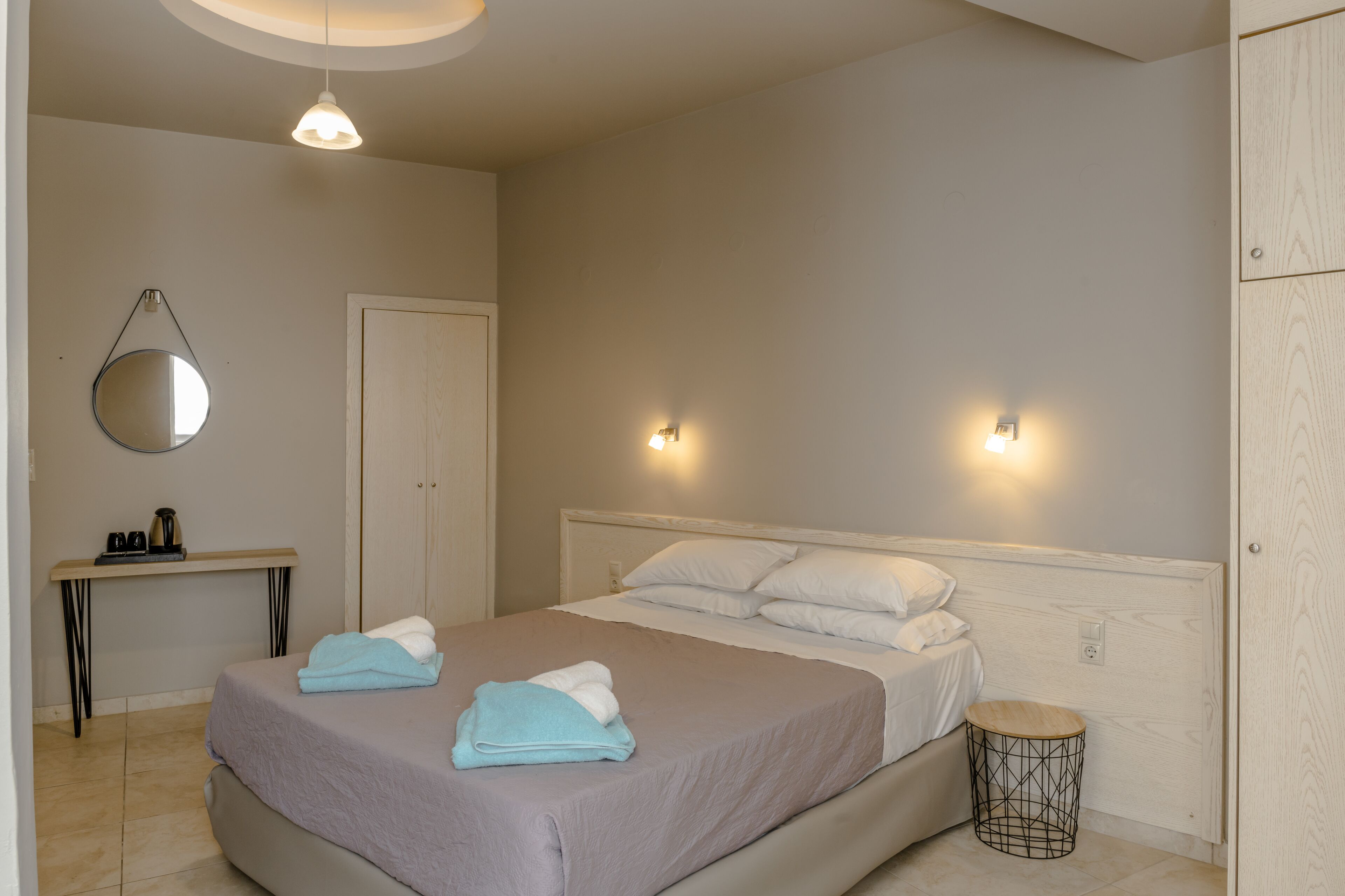 Quarto com cama, mesa de cabeceira, espelho e luminárias fixadas na parede.