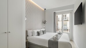 Quarto moderno com uma cama grande, mesa de cabeceira, televisão na parede e vista para a varanda.