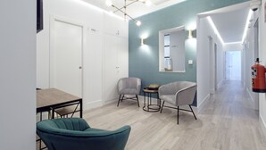 Um interior moderno com uma parede destaque azul-esverdeado, uma área de refeições com mesa e cadeiras, e um corredor que dá para outro quarto.