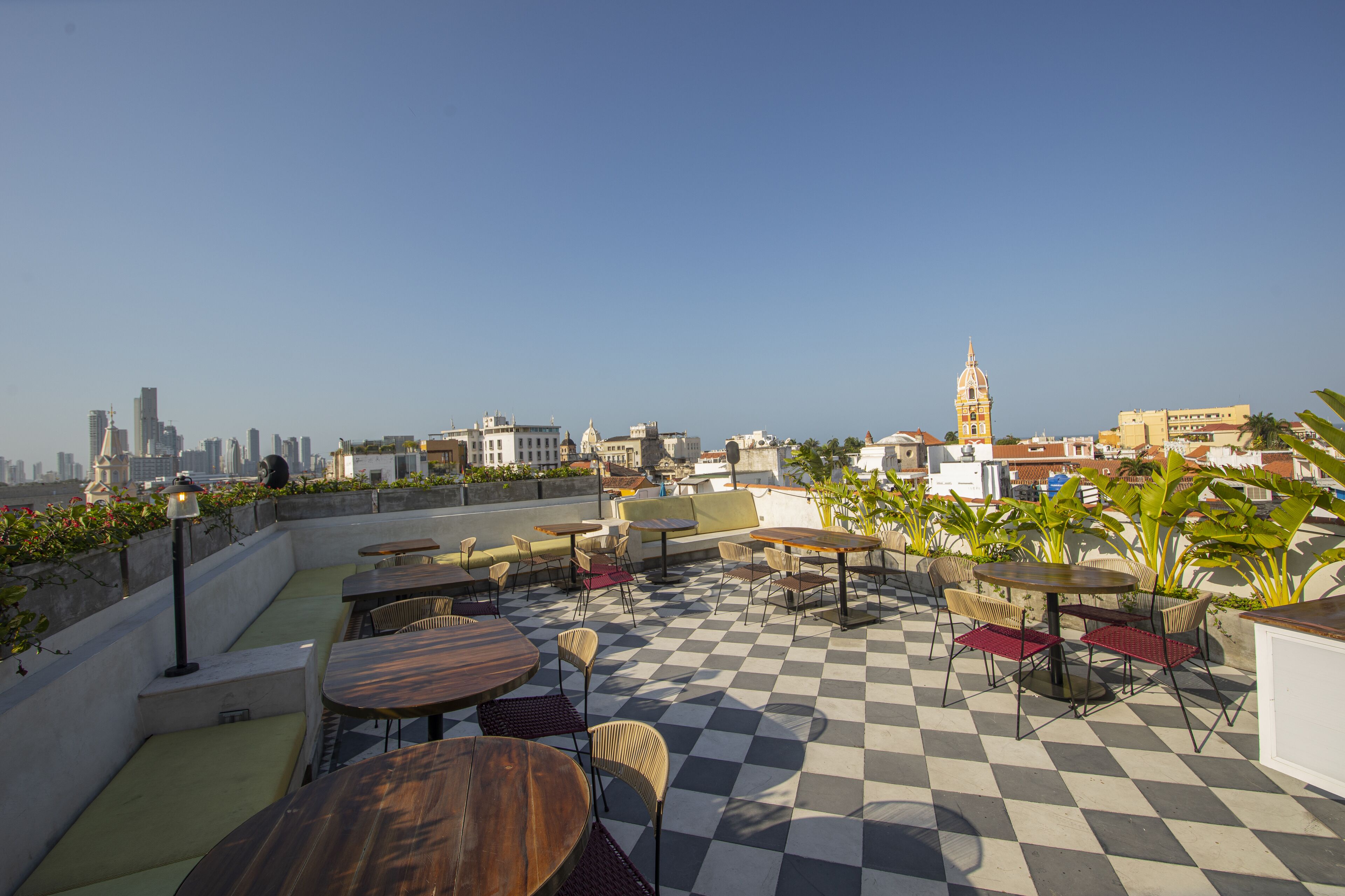 Terraço no telhado com piso xadrez, áreas de estar e vista para o horizonte urbano.