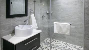 Uma casa de banho moderna com cabine de duche em vidro, lavatório branco e chão em azulejos.