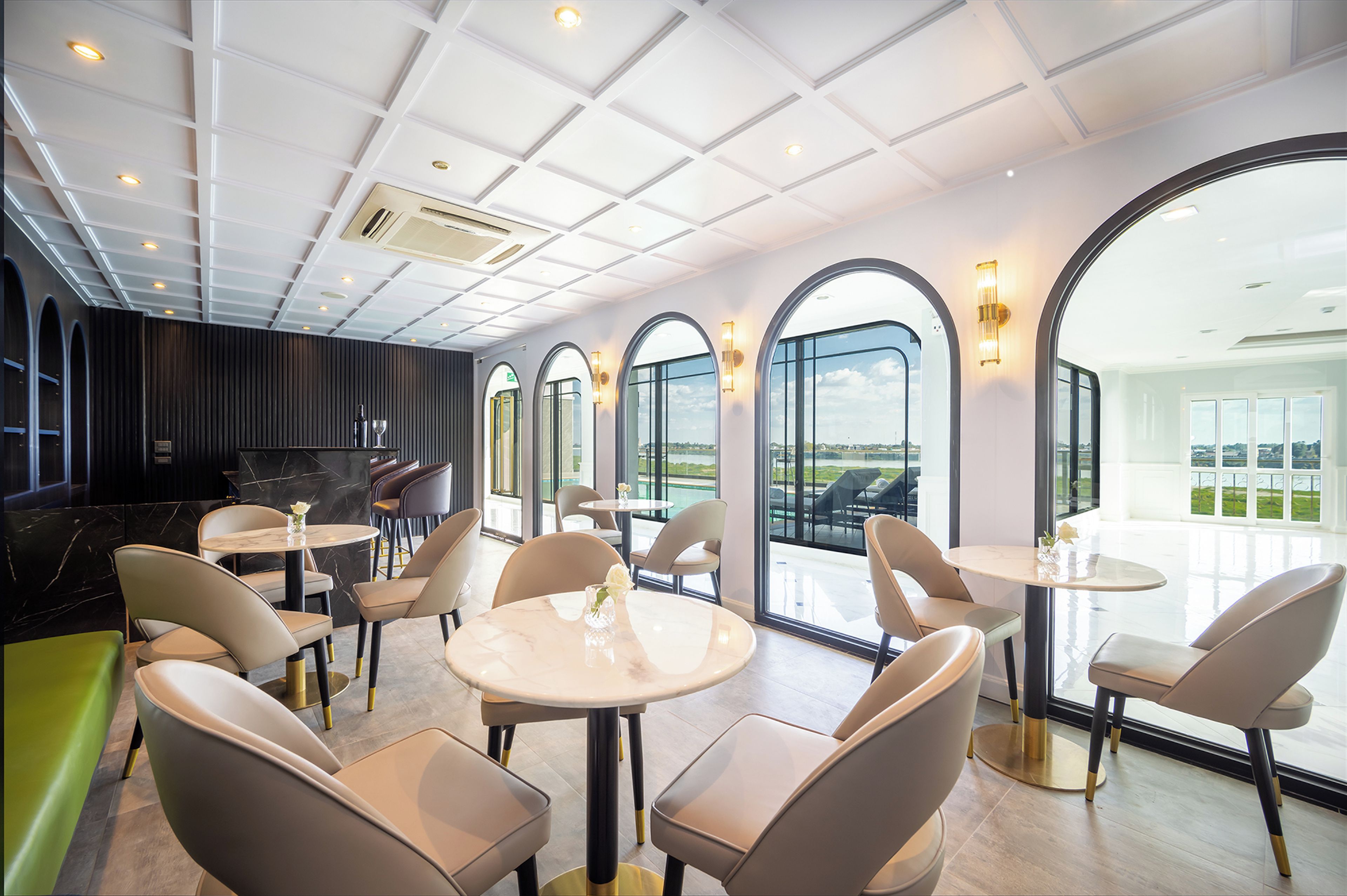 Uma zona de refeições moderna com mesas e cadeiras redondas, janelas em arco grandes e vista para o exterior.