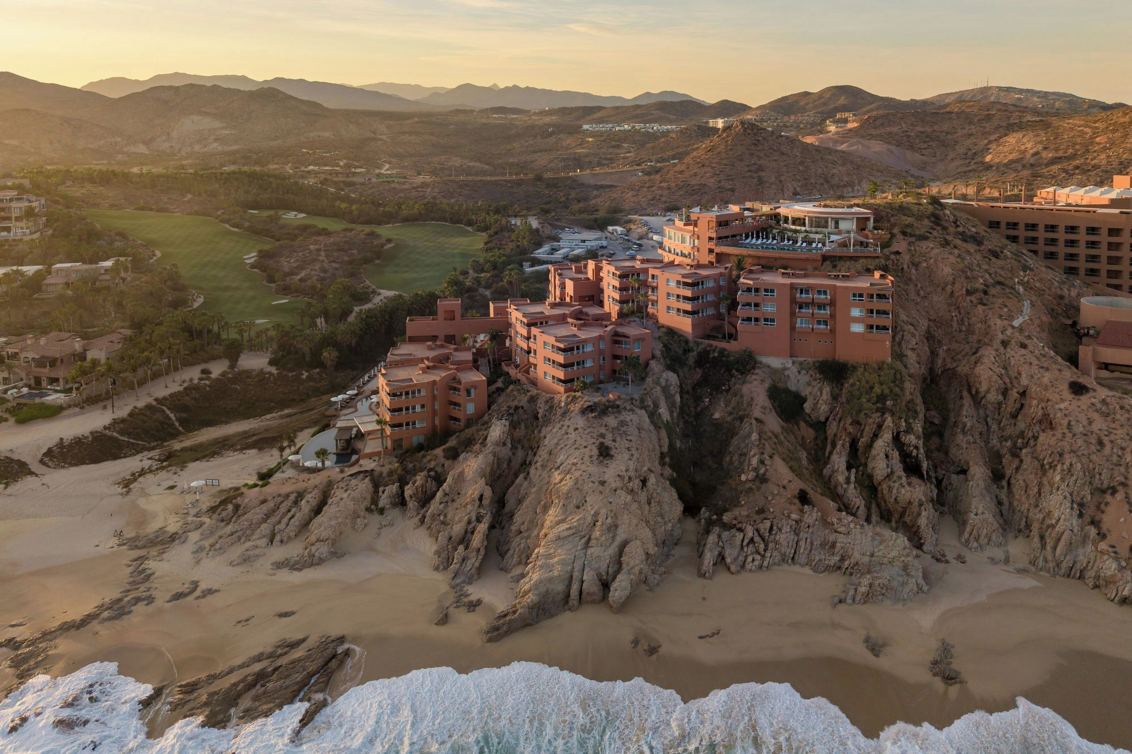 Um hotel à beira-mar com vários edifícios, uma praia e um campo de golfe ao fundo.