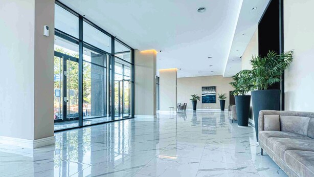 Um hall amplo com grandes portas de vidro, piso de mármore polido e área de estar com sofá e plantas em vasos.