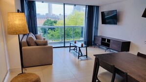 Uma sala de estar moderna com sofá, mesa de jantar, televisão e vista da cidade através de grandes janelas.