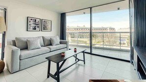 Uma sala de estar moderna com um sofá cinzento, uma mesa de centro e uma grande janela com vista para a cidade.