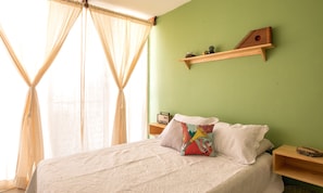 Um quarto com cama, mesa de cabeceira, rádio e prateleira com objetos decorativos.