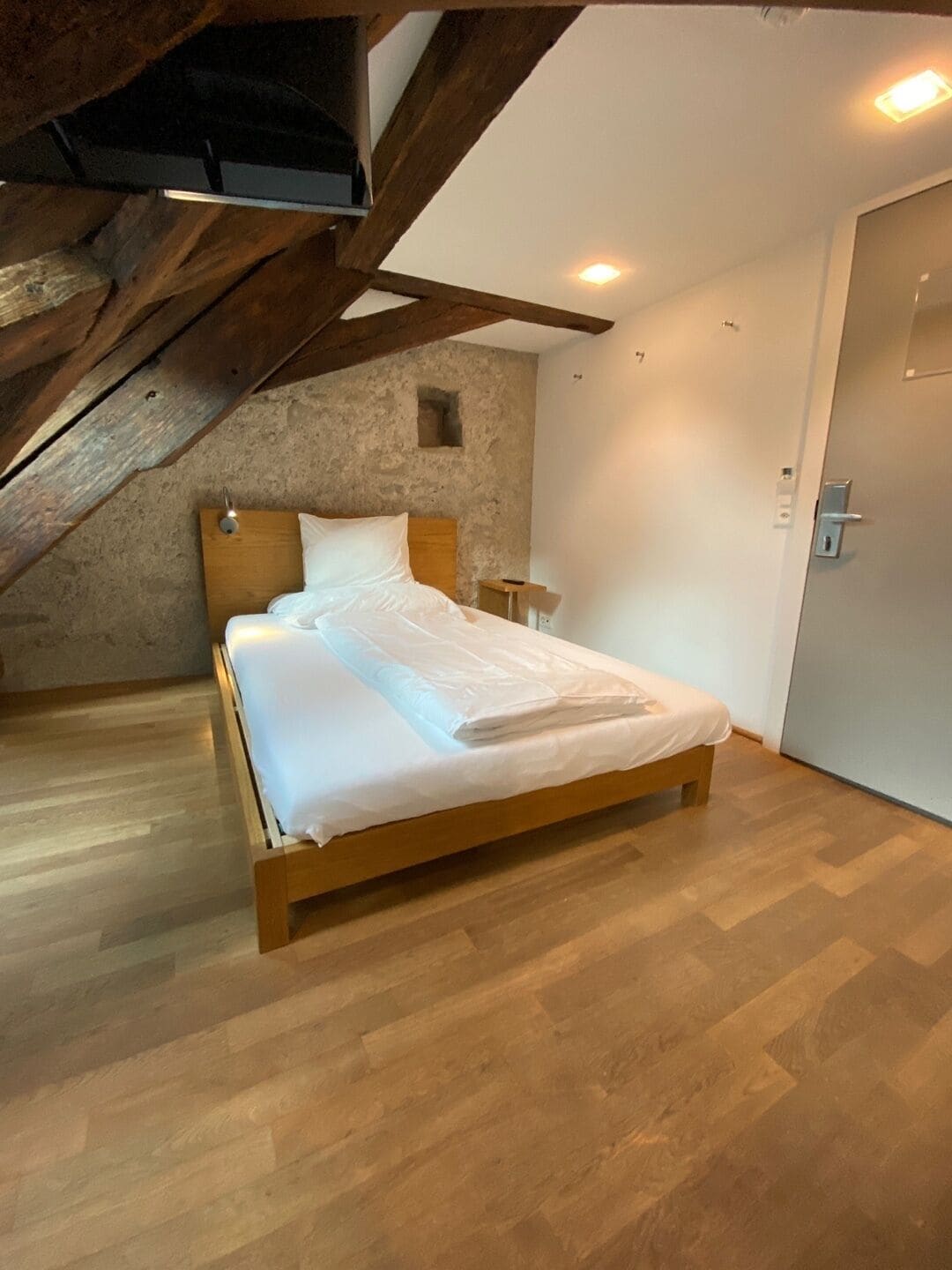 Quarto com cama de madeira, parede de pedra e teto inclinado.