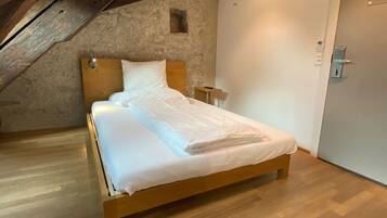 Quarto com cama de madeira, parede de pedra e teto inclinado.