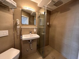 Uma casa de banho moderna com chuveiro de vidro, pia branca e secador de cabelo fixado na parede.