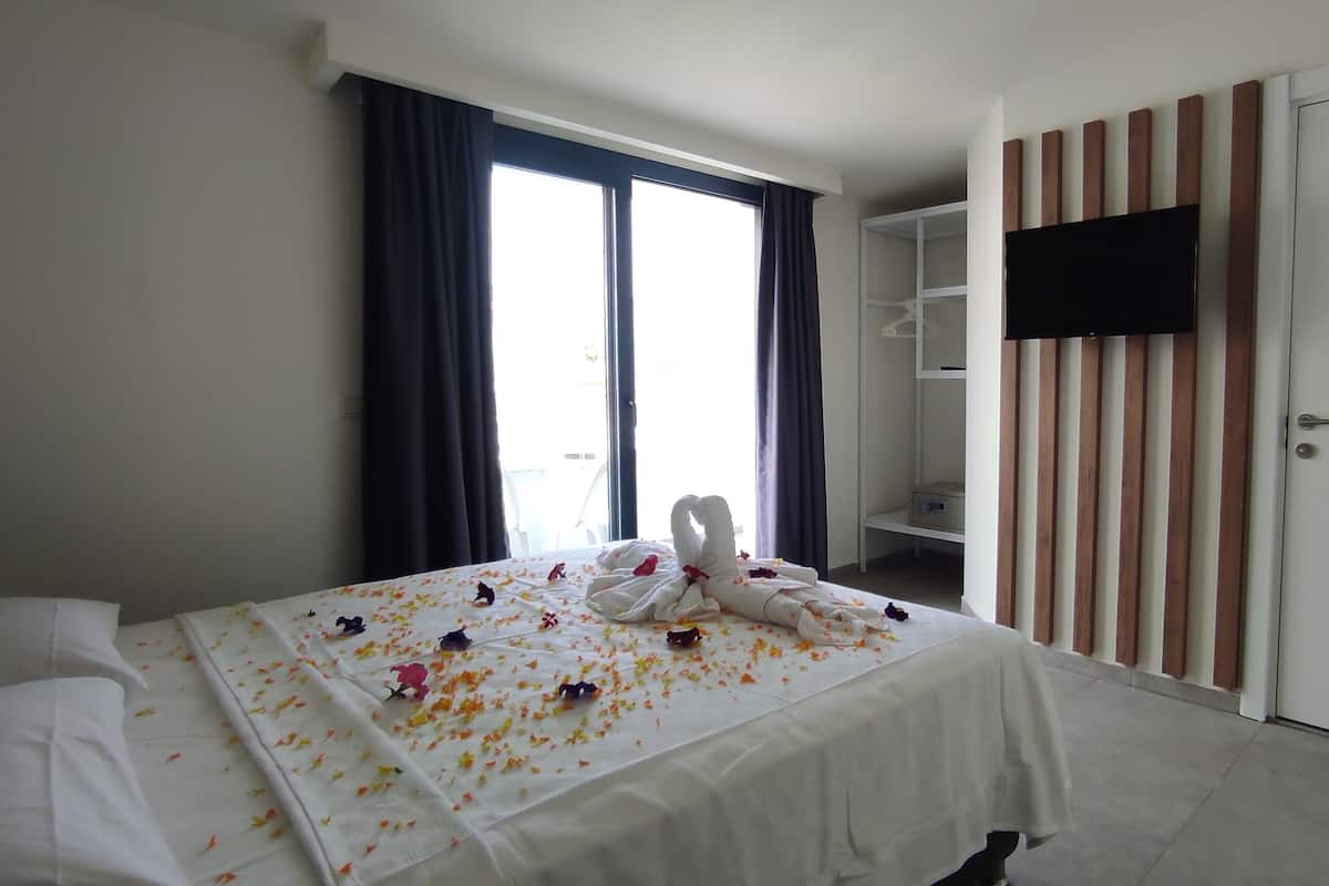 Quarto de hotel com uma cama, televisão presa na parede e um guarda-roupa.