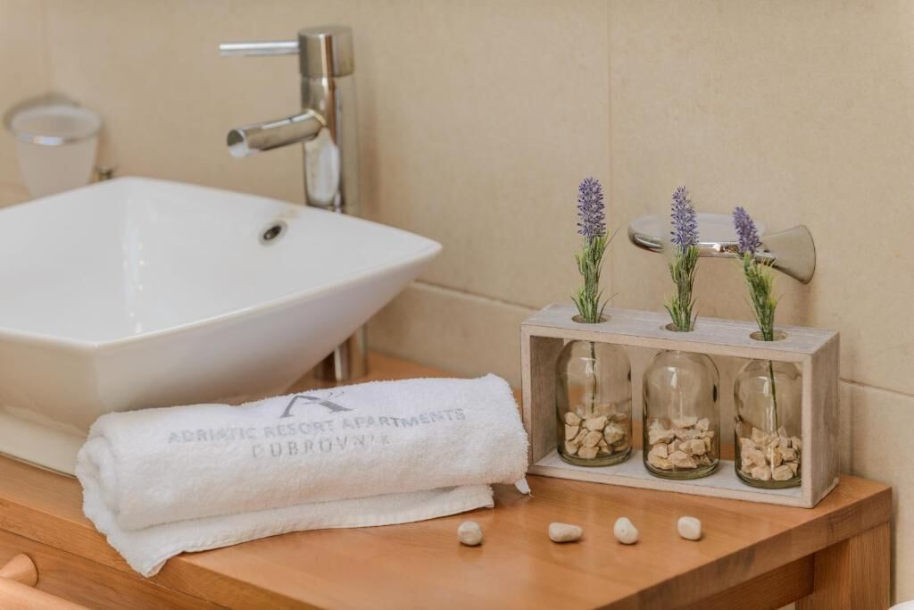 Casa de banho com lavatório branco, toalha com texto e frascos decorativos com lavanda e pedras.