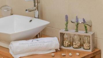 Casa de banho com lavatório branco, toalha com texto e frascos decorativos com lavanda e pedras.