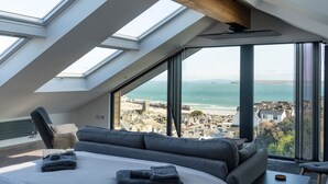 Quarto com pé direito alto, janelas no teto e vista para o mar e a cidade.