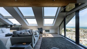 Quarto moderno no estilo loft, com janelas do teto, sofá, poltrona e vista da cidade.