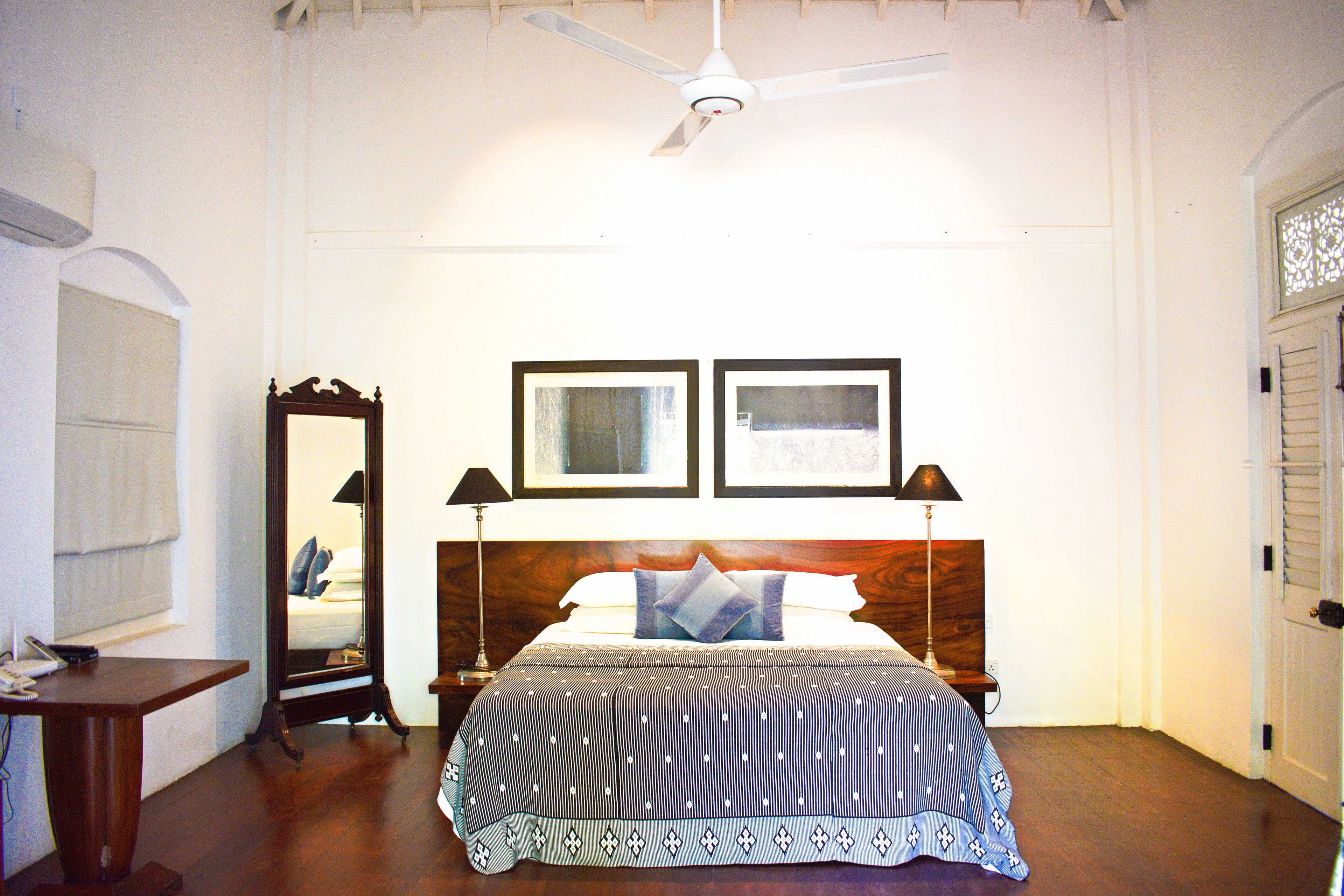 Um quarto bem arrumado com uma cama de madeira, uma mesa de cabeceira, um espelho e duas molduras com fotos na parede.
