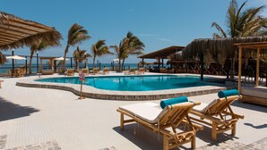 Uma área à beira da piscina com espreguiçadeiras, piscina e palmeiras.