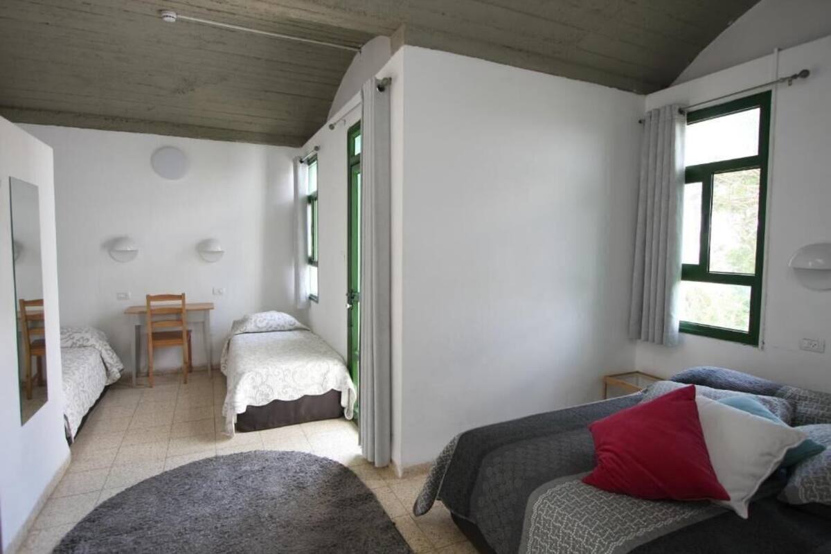 Quarto com duas camas, uma escrivaninha, uma cadeira e uma janela com cortinas.