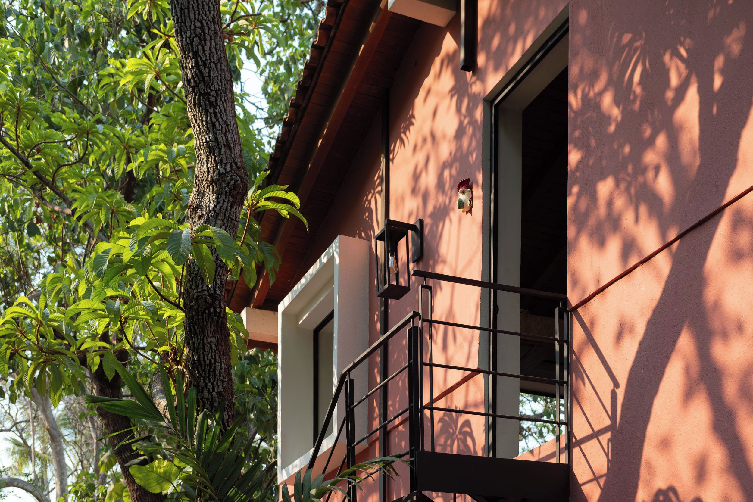 Um edifício com fachada vermelha, uma janela e uma árvore com folhas verdes.