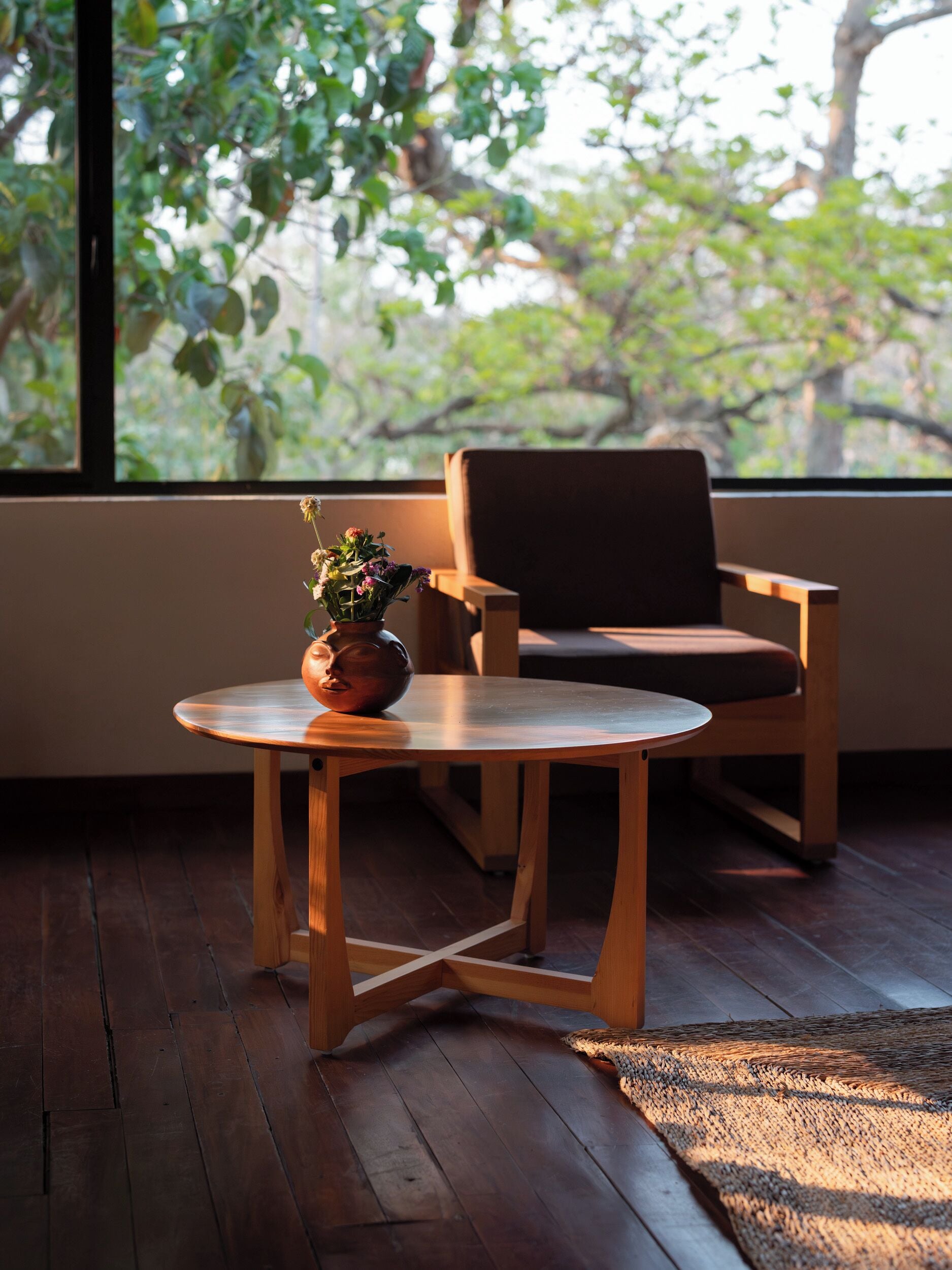 Um quarto com piso de madeira, uma mesa redonda com um vaso de planta e uma cadeira marrom.