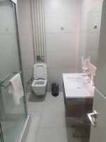 Casa de banho moderna com cabine de duche em vidro, sanita, lavatório e um contentor de lixo.