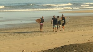 Uma praia com pessoas caminhando e carregando pranchas de surf.