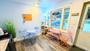 Quarto com piso de madeira, mesa redonda com cadeiras, janela com vista e uma porta.