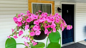 Um arranjo de flores pendurado em frente a uma casa com uma porta marcada com o número 5 e uma cadeira verde.