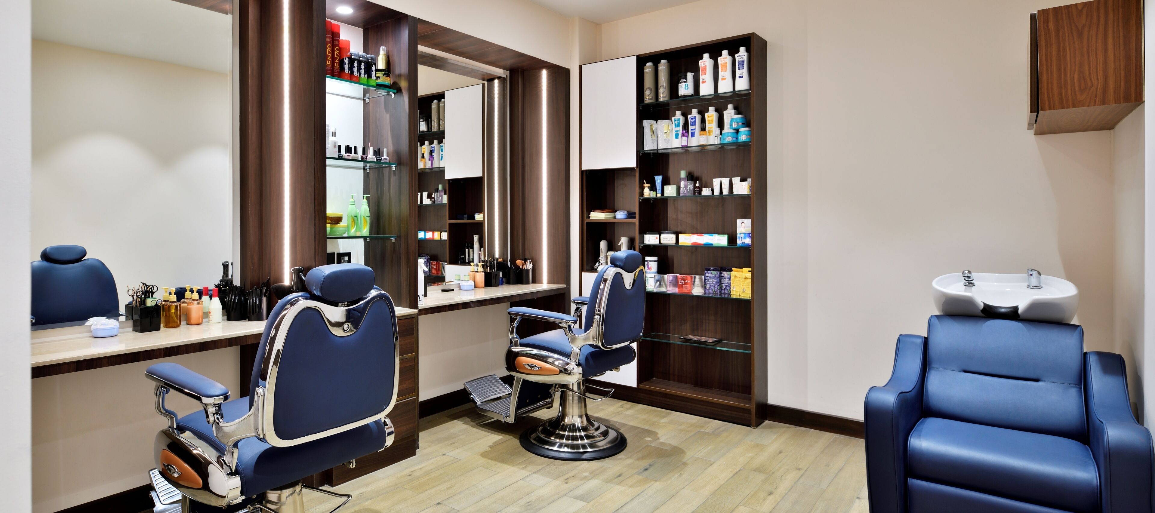 Um salão moderno com duas cadeiras de barbeiro azuis, um espelho grande e prateleiras repletas de produtos para cabelo.