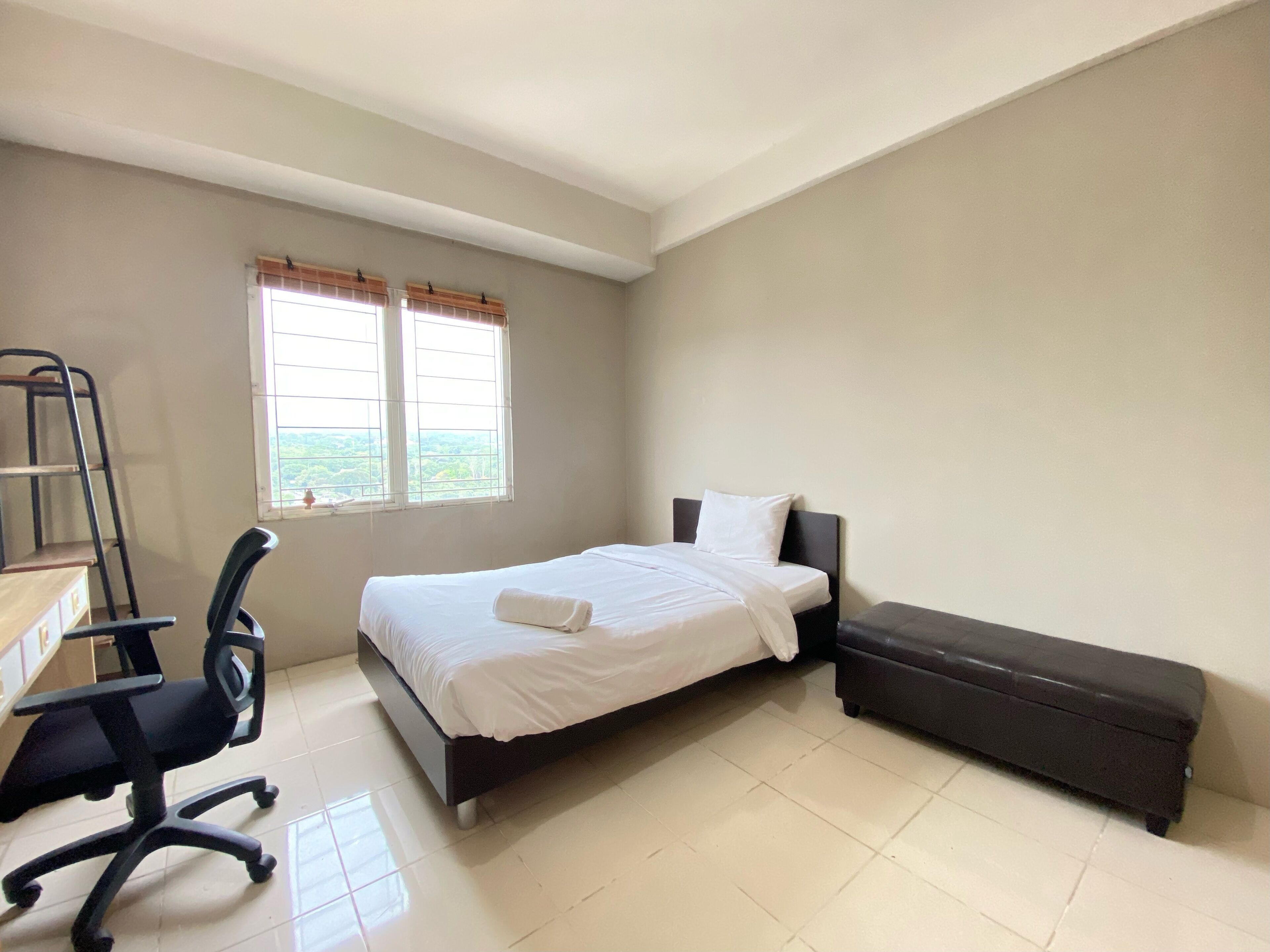 Quarto com cama, escrivaninha, cadeira, banco e janela com cortinas.
