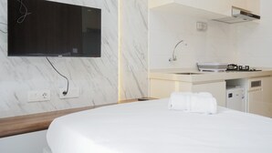 Quarto de hotel moderno com uma cama grande, televisão de tela plana na parede, pia embutida e uma pequena cozinha.