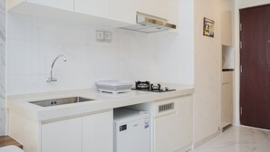 Uma cozinha moderna com armários brancos, uma pia de aço inoxidável, um mini-refrigerador embutido e um fogão a gás.