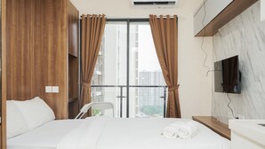 Quarto de hotel com uma cama grande, uma TV fixada na parede e vista para a cidade pela janela.
