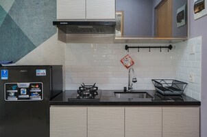 Cozinha com geladeira preta, painel de azulejos brancos, coifa de aço inoxidável, pia e escorredor de louça preto.