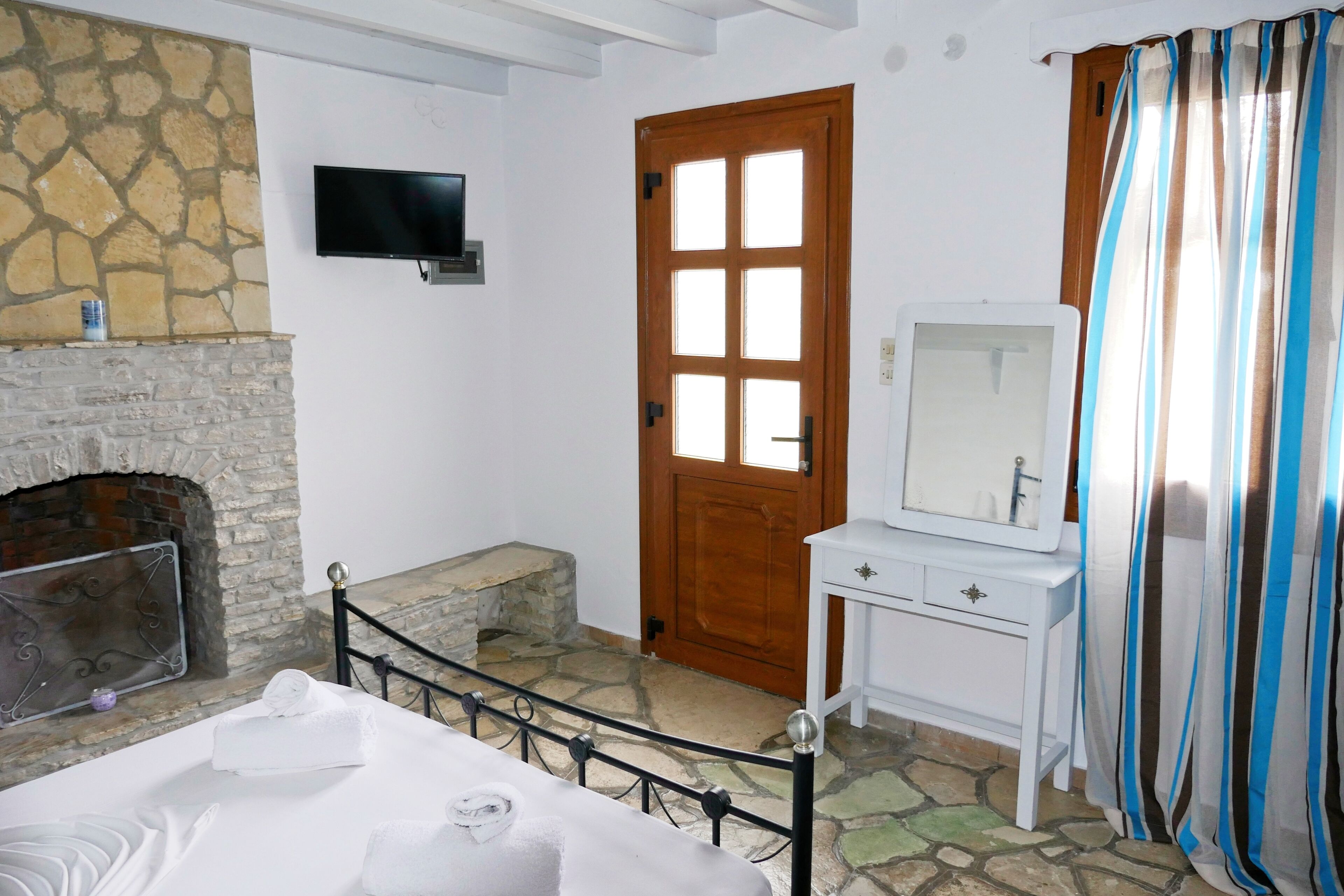Quarto com lareira de pedra, porta de madeira, mesa de cabeceira branca e cortina listrada.