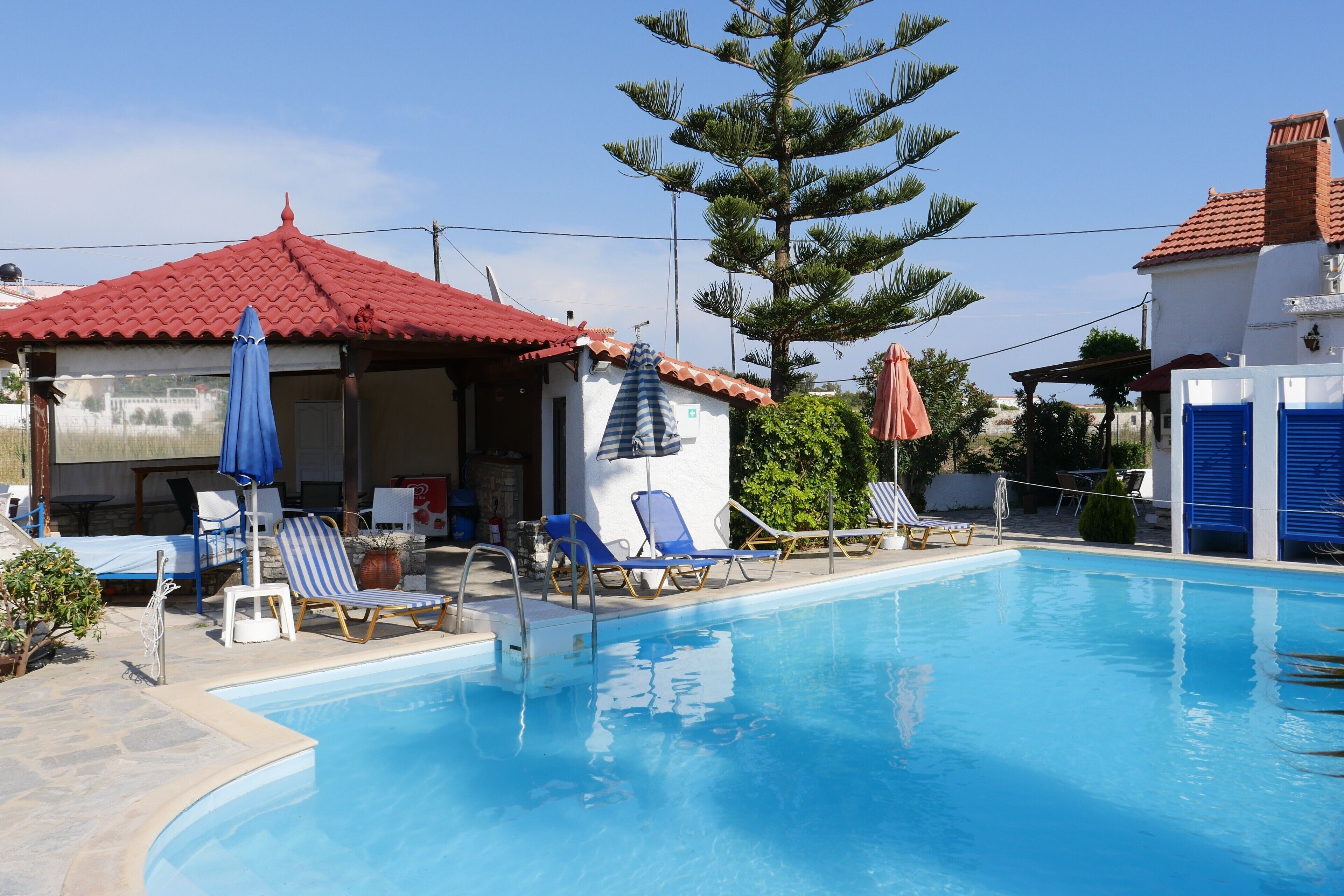 Piscina com espreguiçadeiras e guarda-sóis, cercada por edifícios com telhados vermelhos.