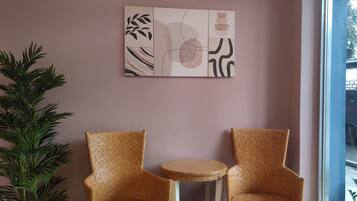 Um quarto com duas cadeiras de vime, uma mesa redonda pequena e um quadro abstrato grande na parede.