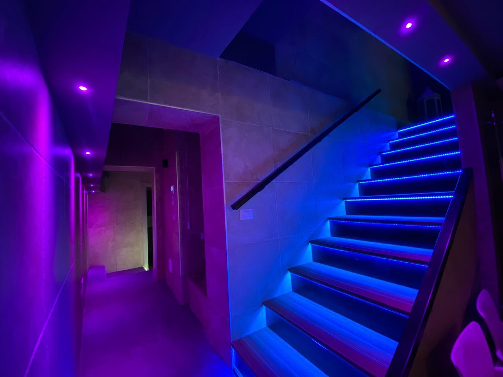 Uma escadaria com iluminação azul em LED, corrimão e parede revestida de azulejos.
