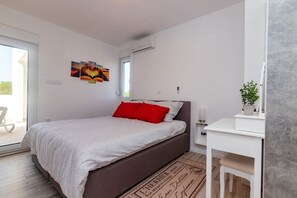 Quarto com uma cama, escrivaninha branca e planta em vaso.