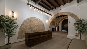 Um hall com um banco de pedra, vigas de madeira e portas em arco.